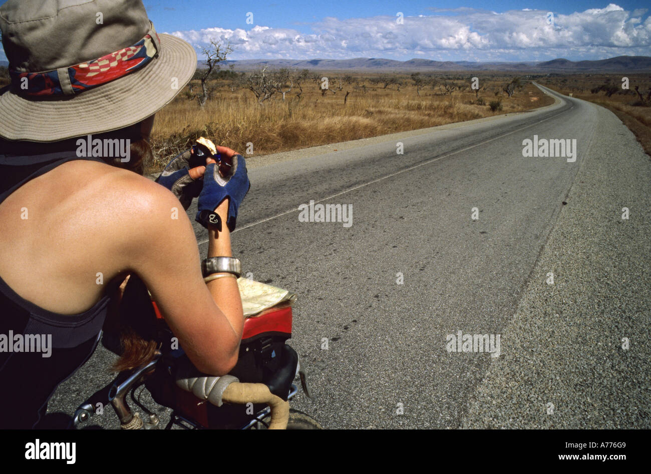 Female cyclist eating bread while leaning on her bicycle on road in ...