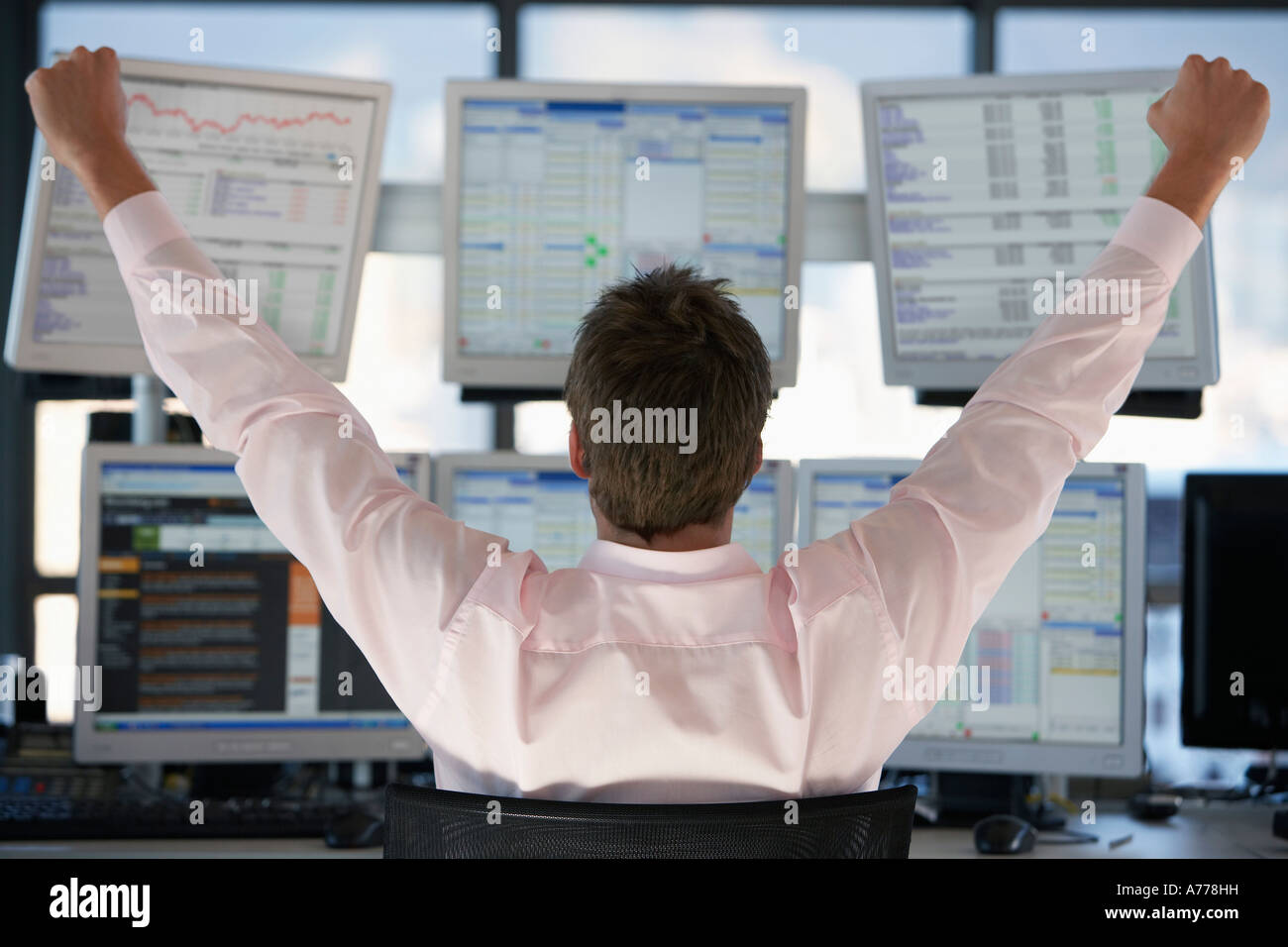 Businessman watching computer screens with arms raised, back view Stock ...