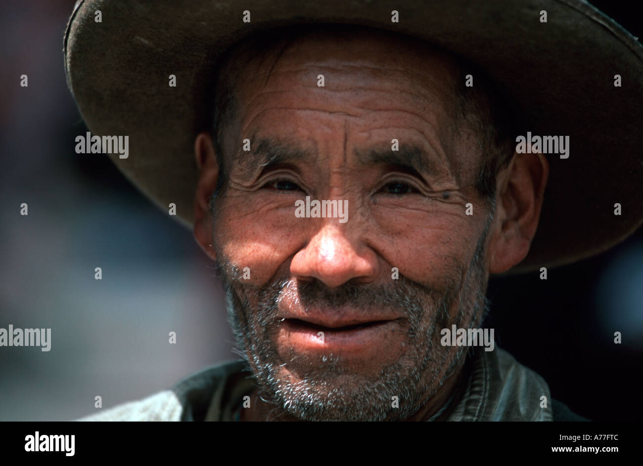 An elderly old wrinkled unshaven smiling man wearing a traditional hat ...
