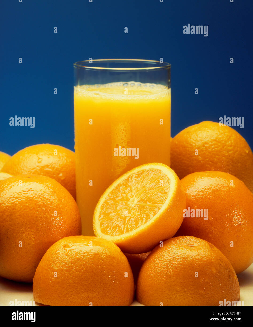 Glass of chilled orange juice in pile of oranges against blue ...