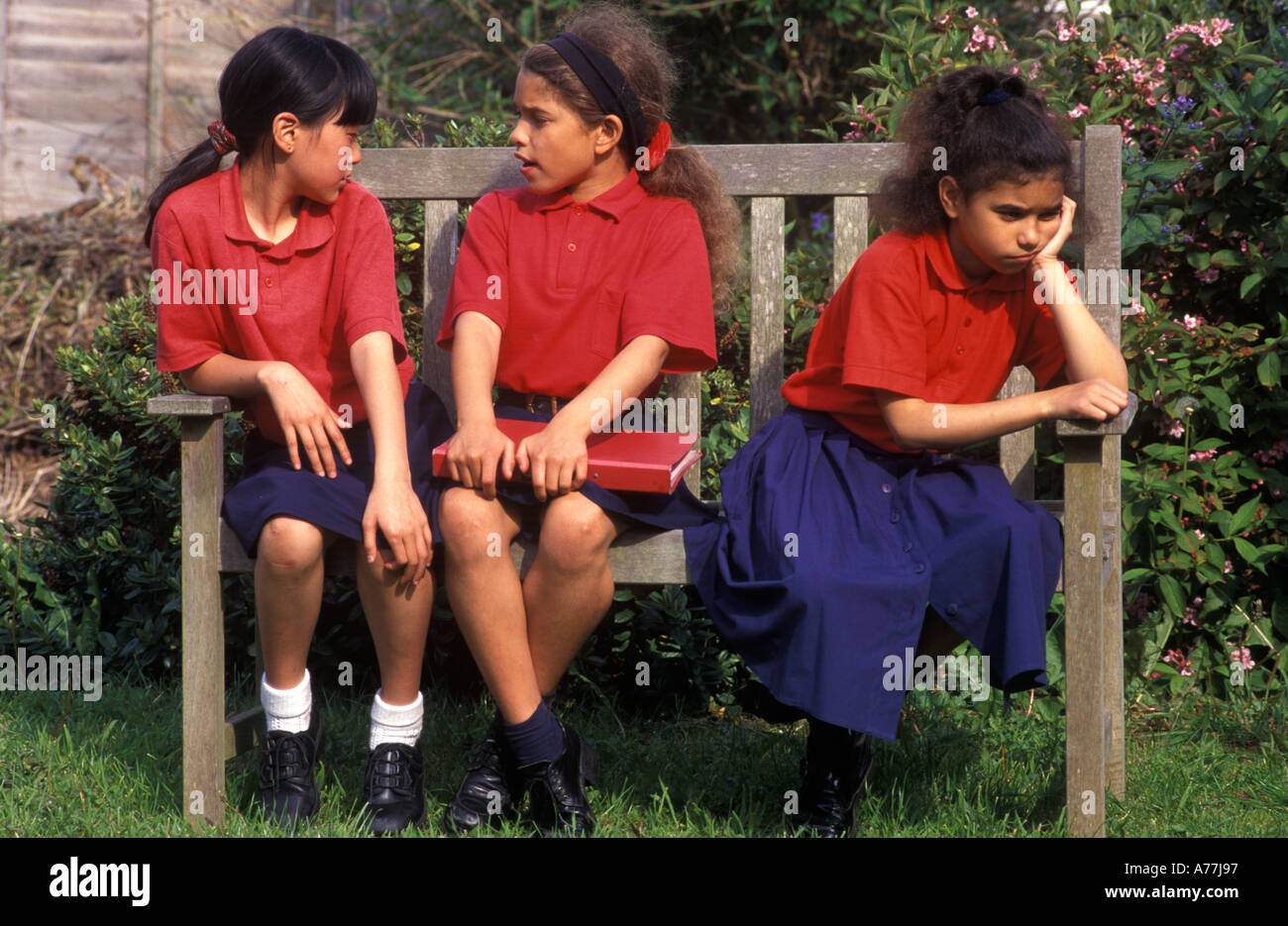 two girls on a bench ignoring their peer who is sulking Stock Photo - Alamy