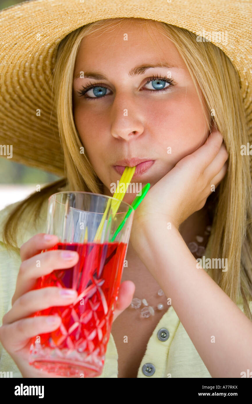 A beautiful young lady drinking a cocktail wearing a straw sun hat and ...