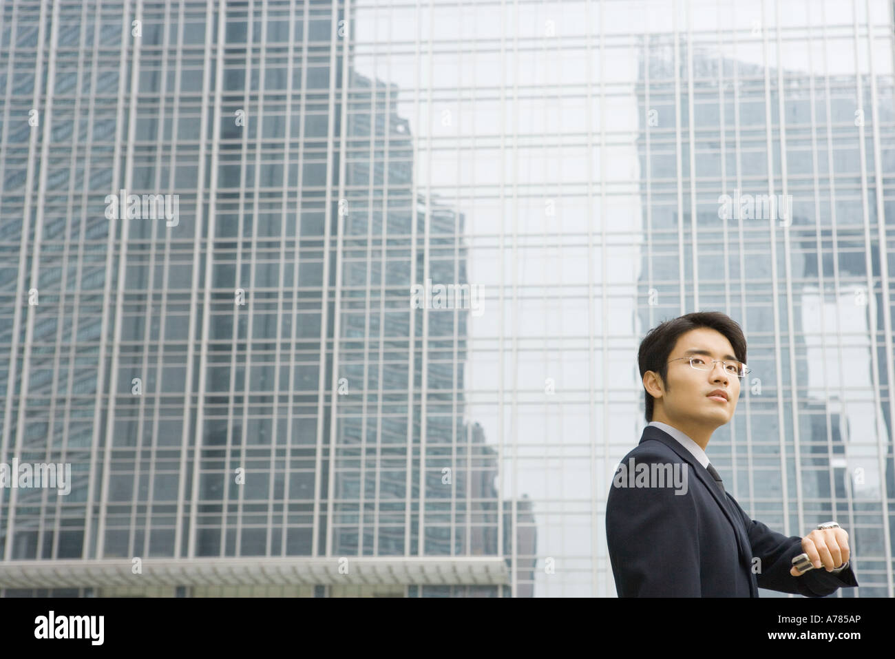 Young businessman holding up wrist to check time, looking away, office ...