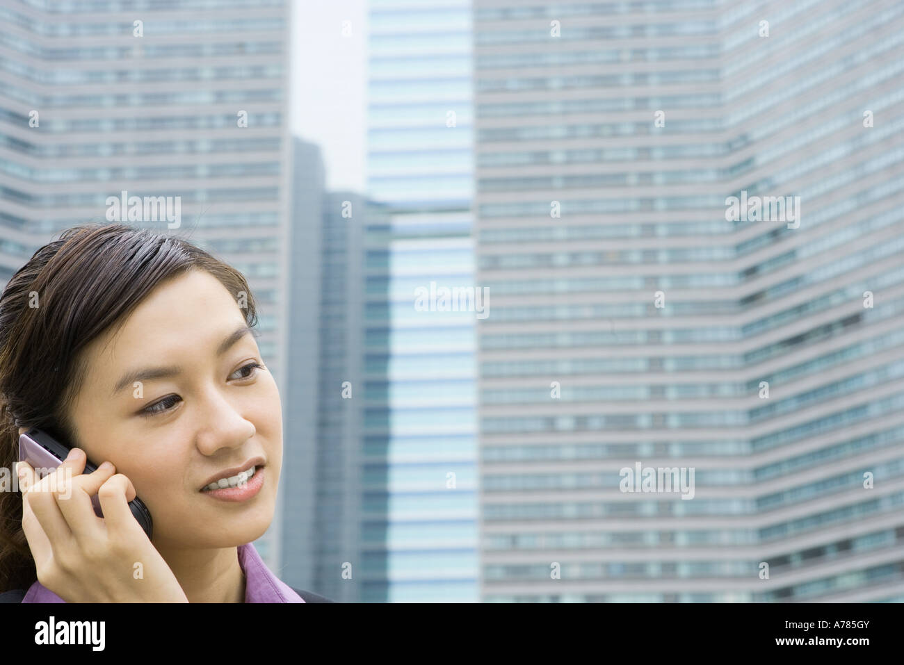 Young businesswoman using cell phone, office buildings in background ...