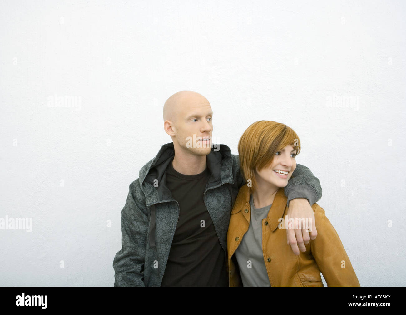 Young couple, man with arm around woman's shoulder, both looking away ...