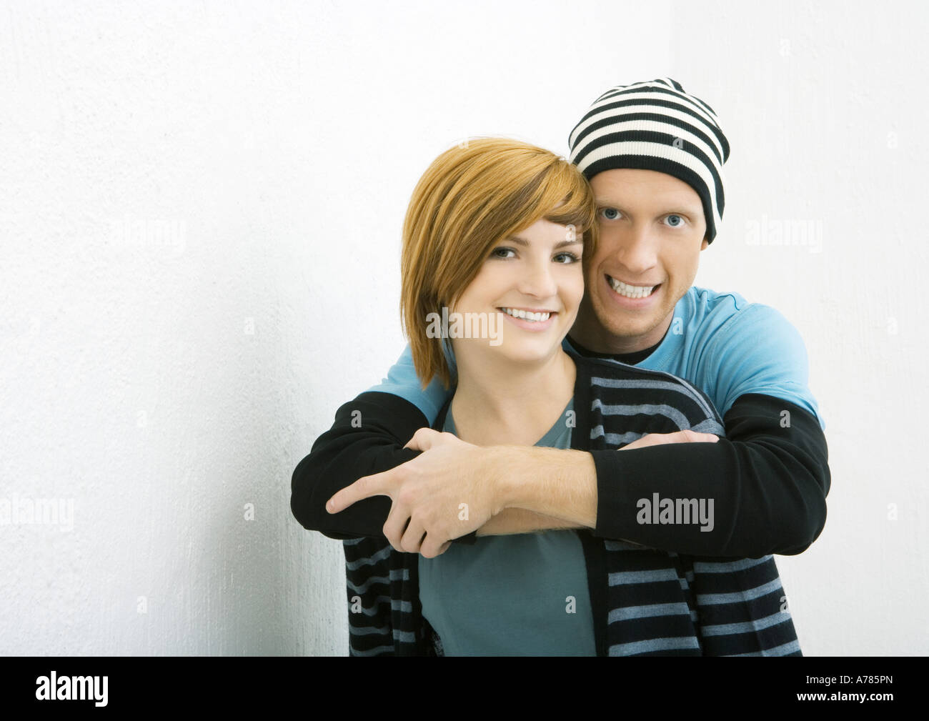 Young couple, man standing behind woman with arms around her, both ...