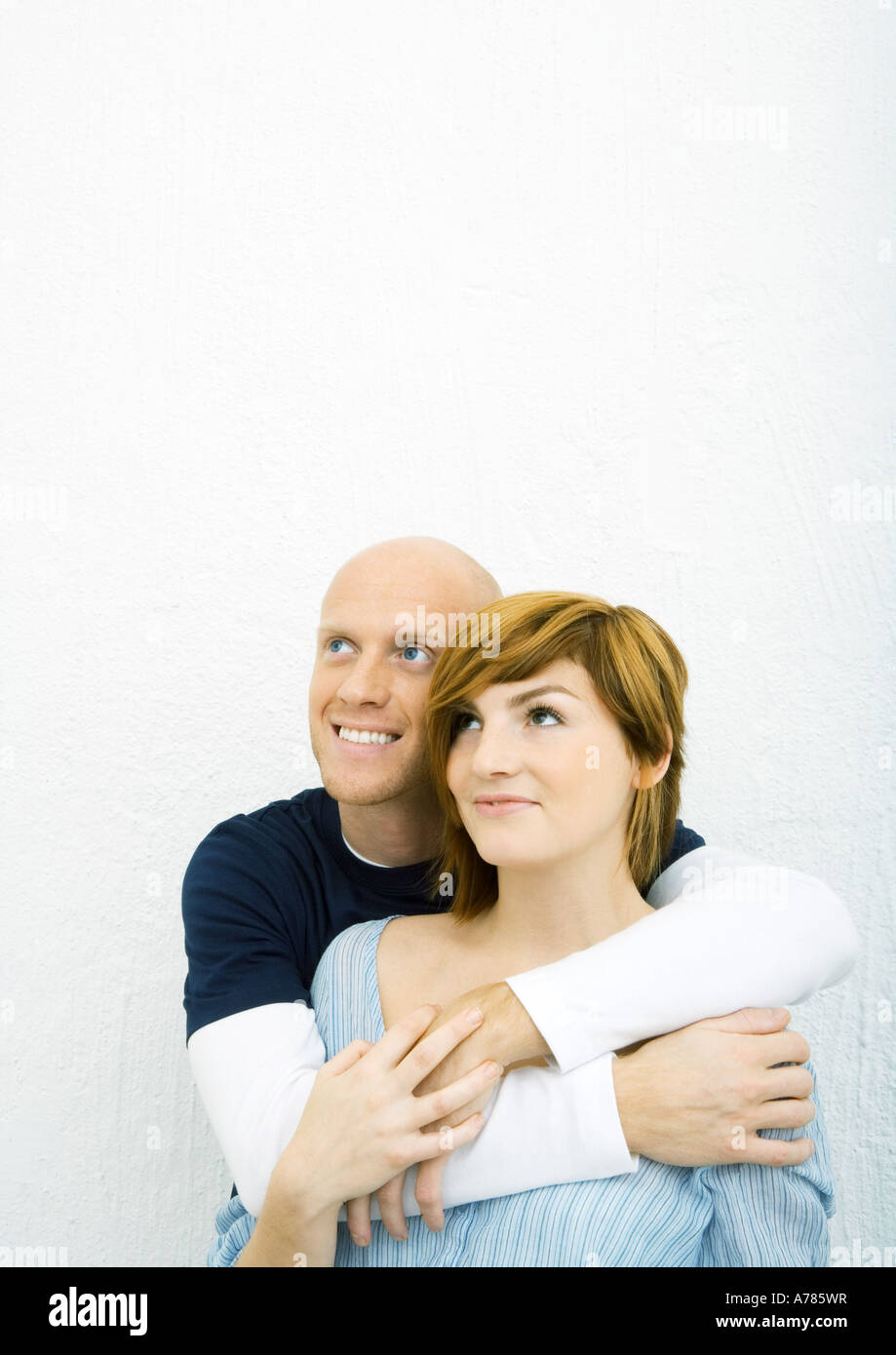 Young couple, man standing behind woman with arms around her, both ...