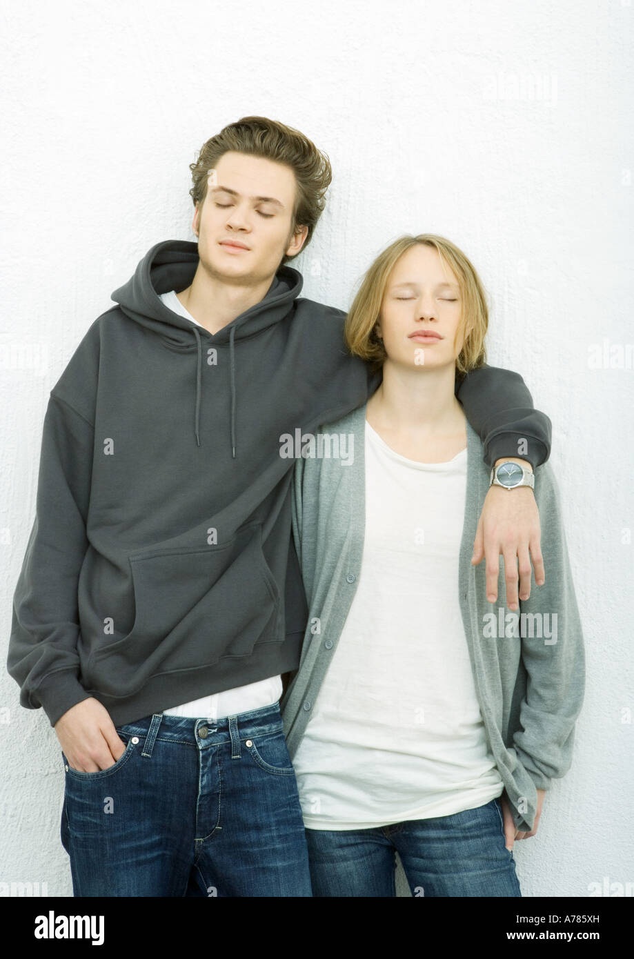 Young couple leaning against wall, man's arm around woman's shoulder ...