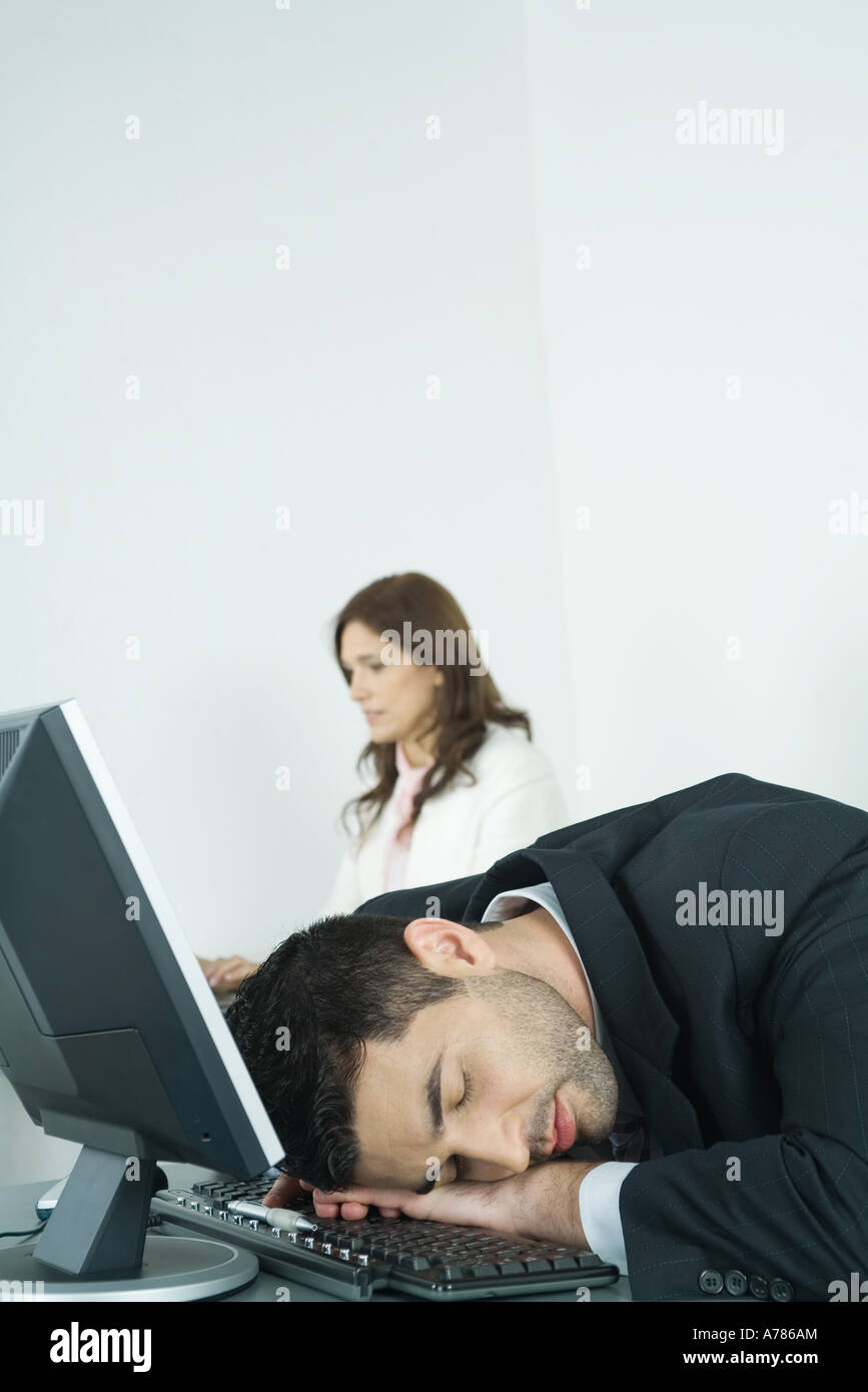 Businessman sleeping on keyboard while colleague works in background ...