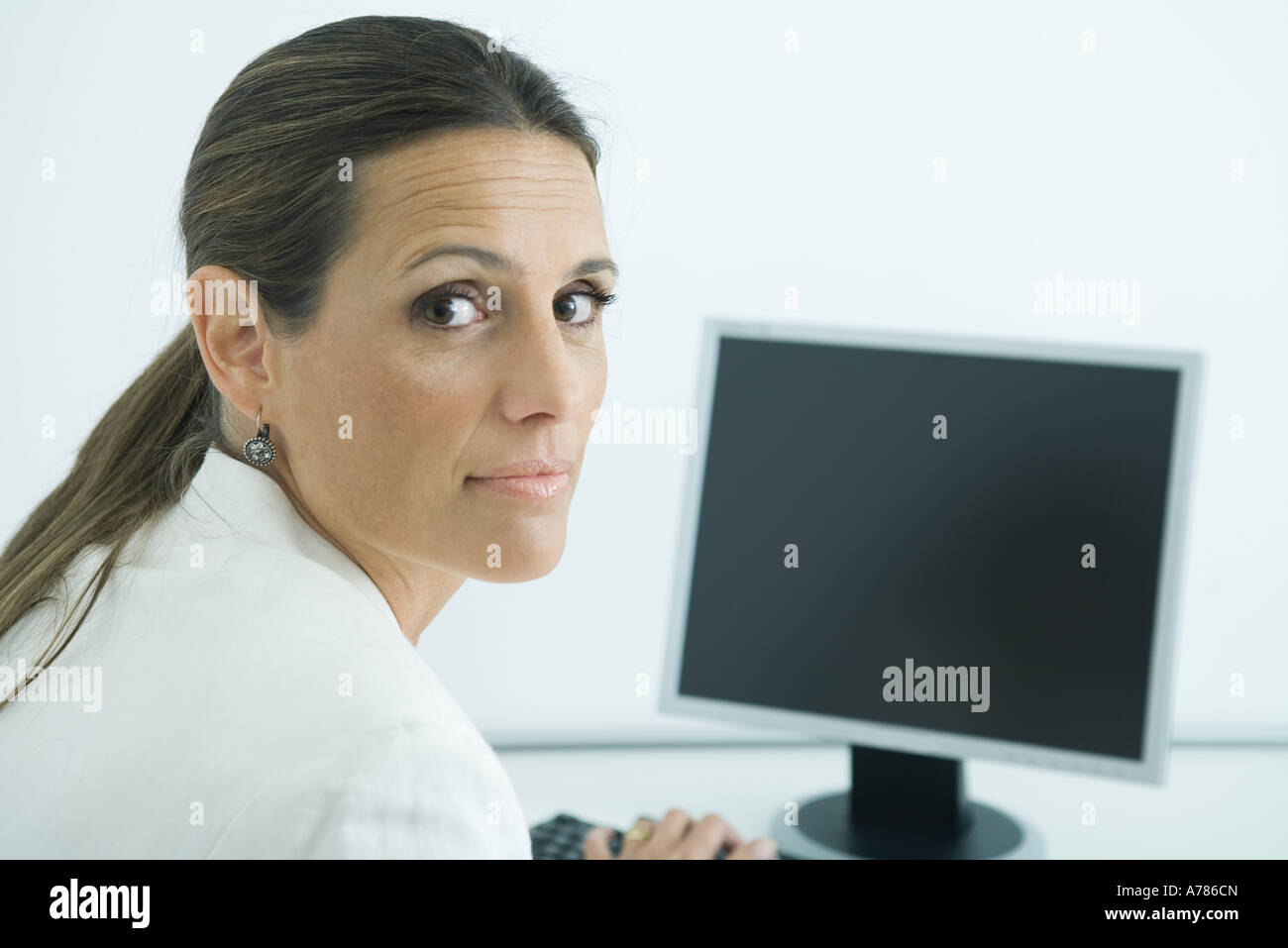 Businesswoman sitting at computer, looking over shoulder at camera ...