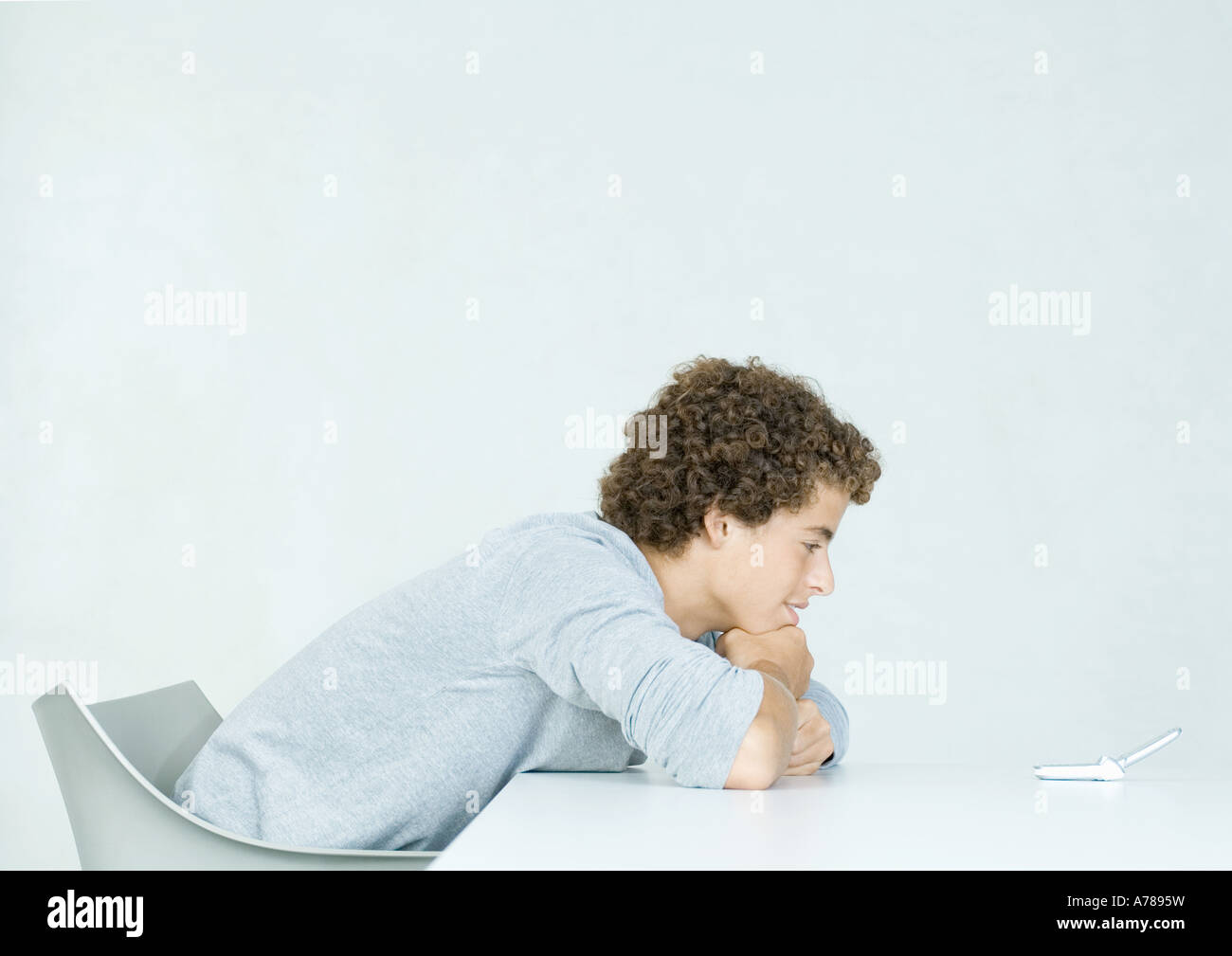 Teenage boy with head down on arms, looking at cell phone Stock Photo ...