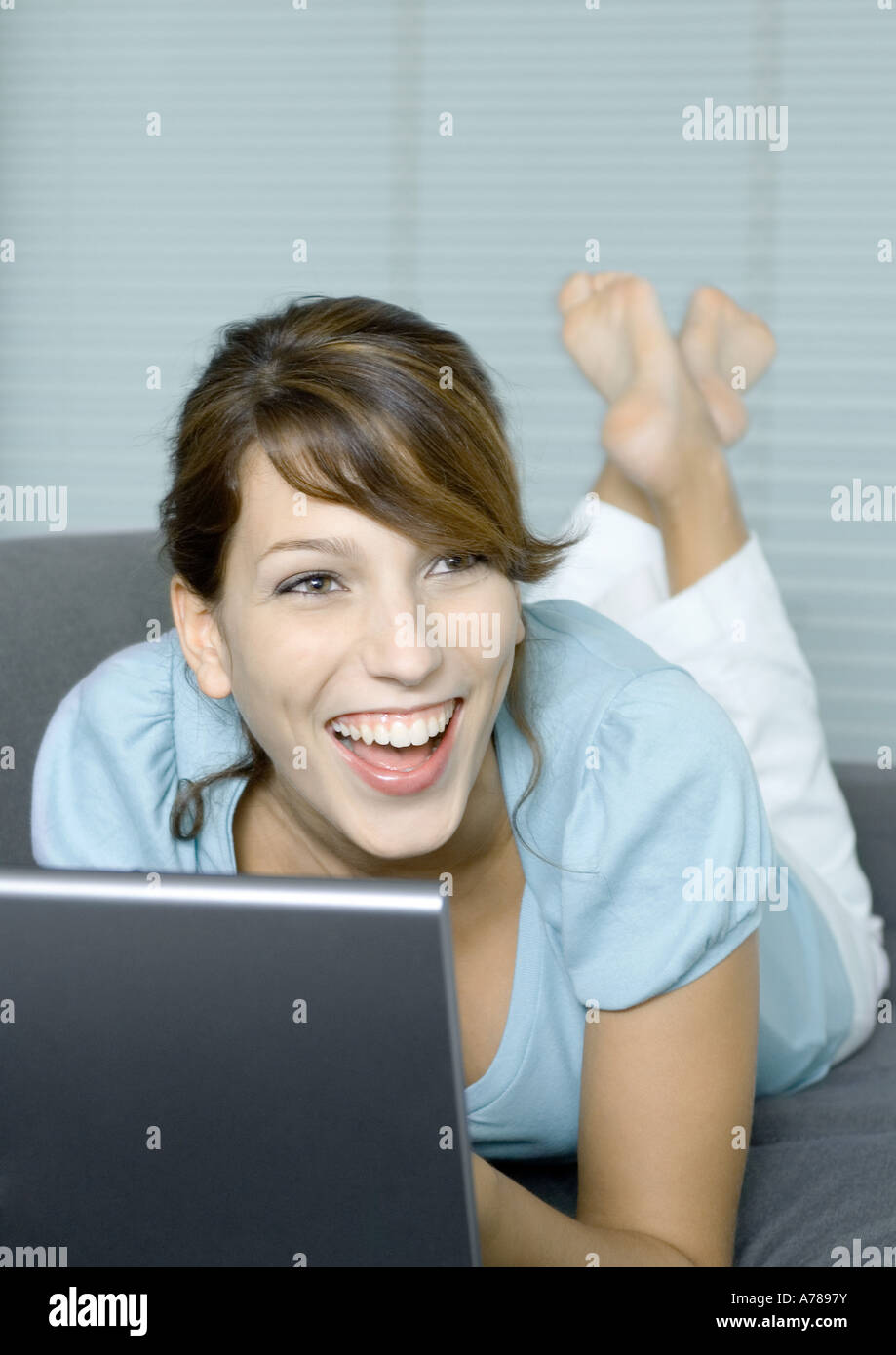 Young woman lying on couch, using laptop, laughing Stock Photo - Alamy