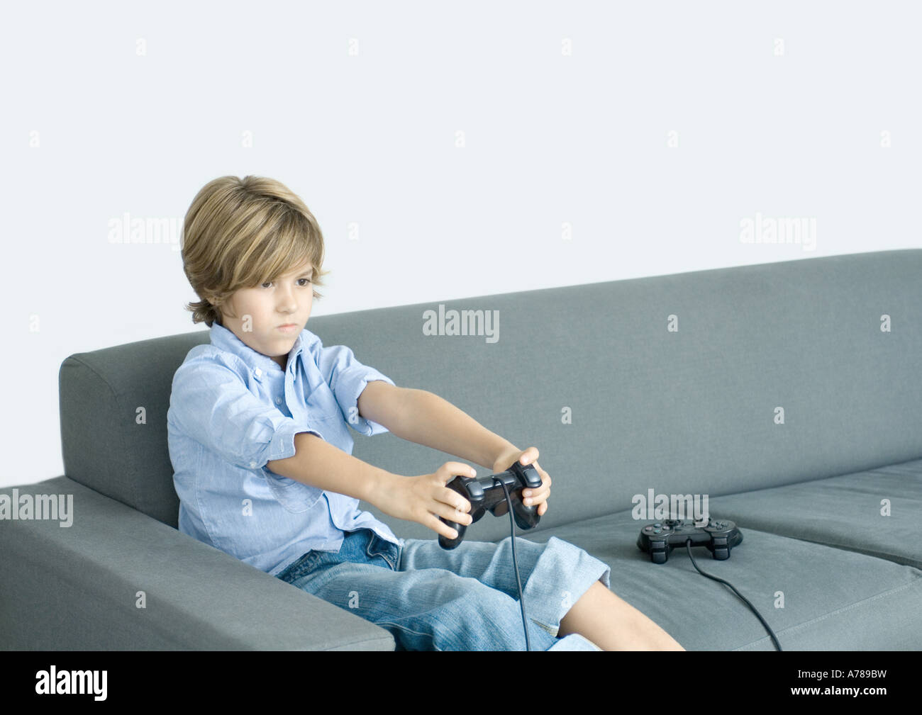 Boy sitting on couch playing video game, scowling Stock Photo - Alamy