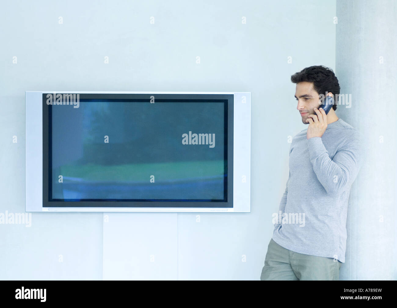 Man leaning against wall using phone, next to widescreen TV Stock Photo ...