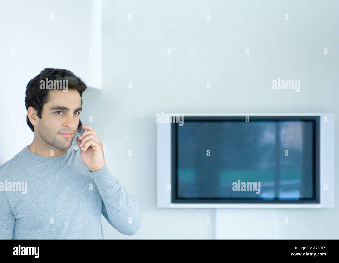 Man using phone, widescreen TV in background Stock Photo - Alamy