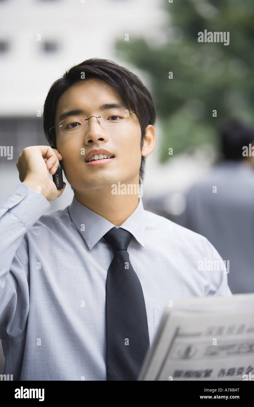Businessman with newspaper using cell phone, looking at camera Stock ...