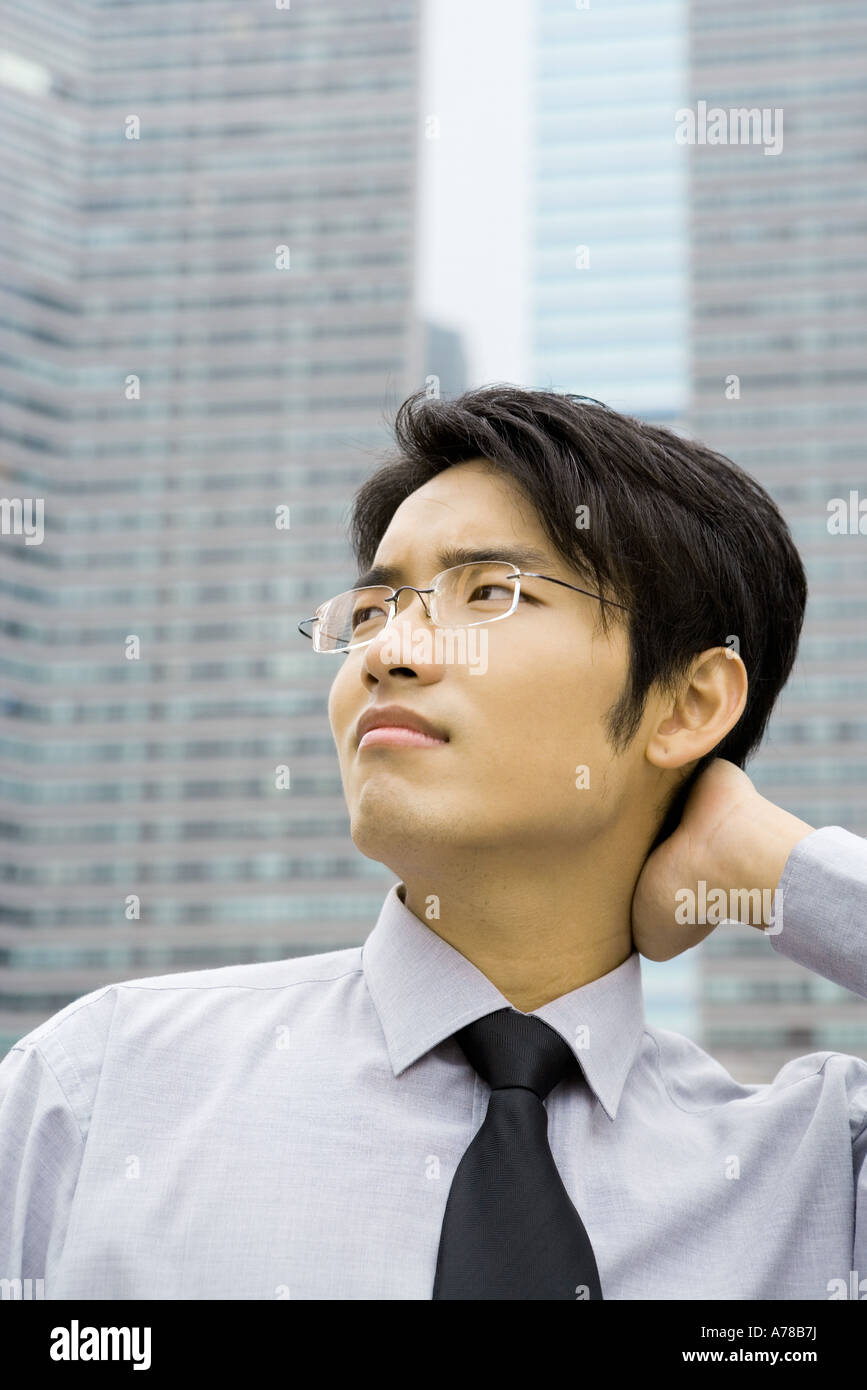 Businessman with hand on back of neck, looking up and frowning Stock ...