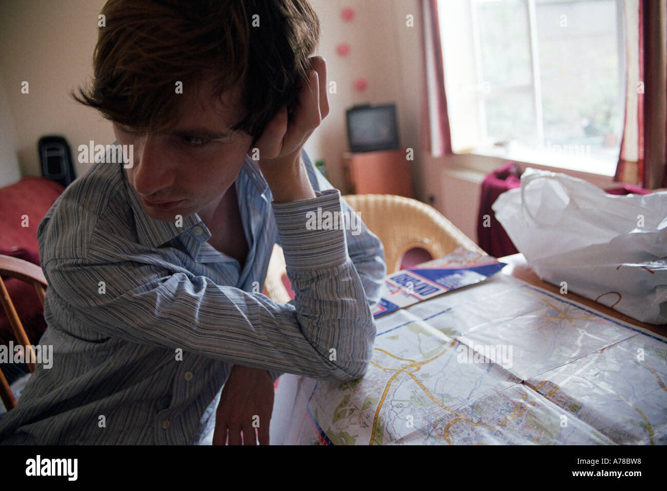Portrait of a sad young man sitting over a map Stock Photo - Alamy