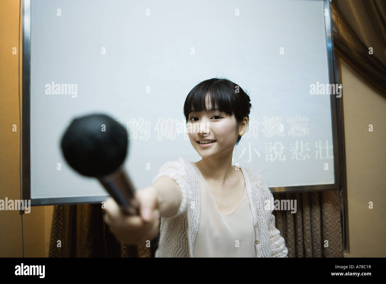 Young woman singing karaoke, holding out microphone toward camera Stock ...