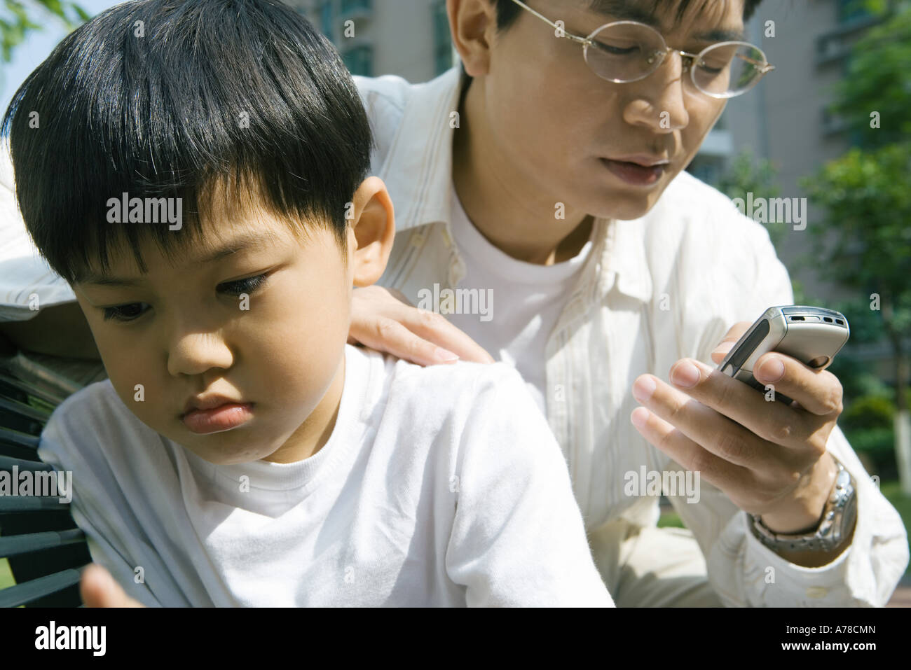 Man looking at cell phone while son looks away, frowning Stock Photo ...