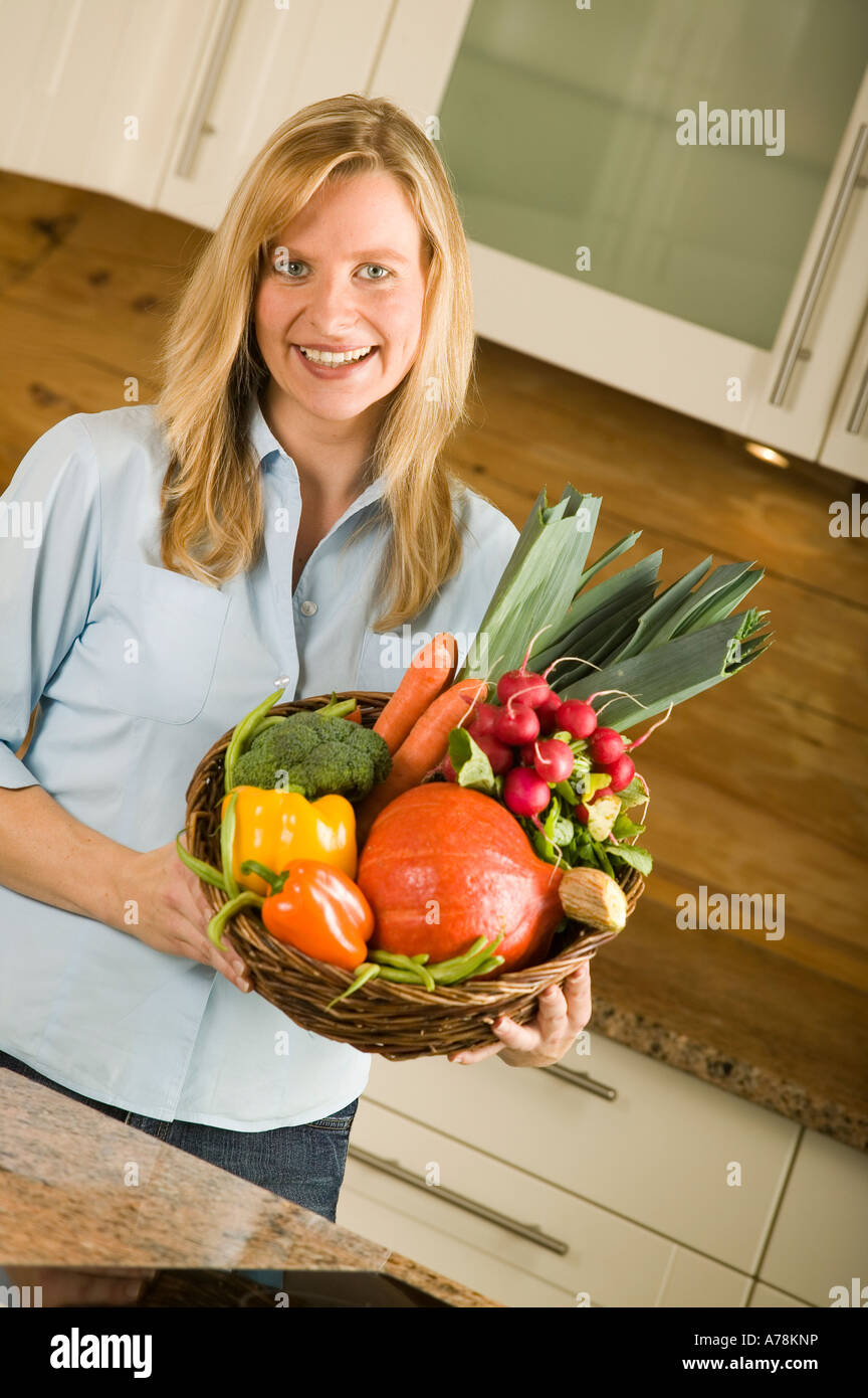 smiling woman in kitchen holding basket with organic vegetables fruit ...