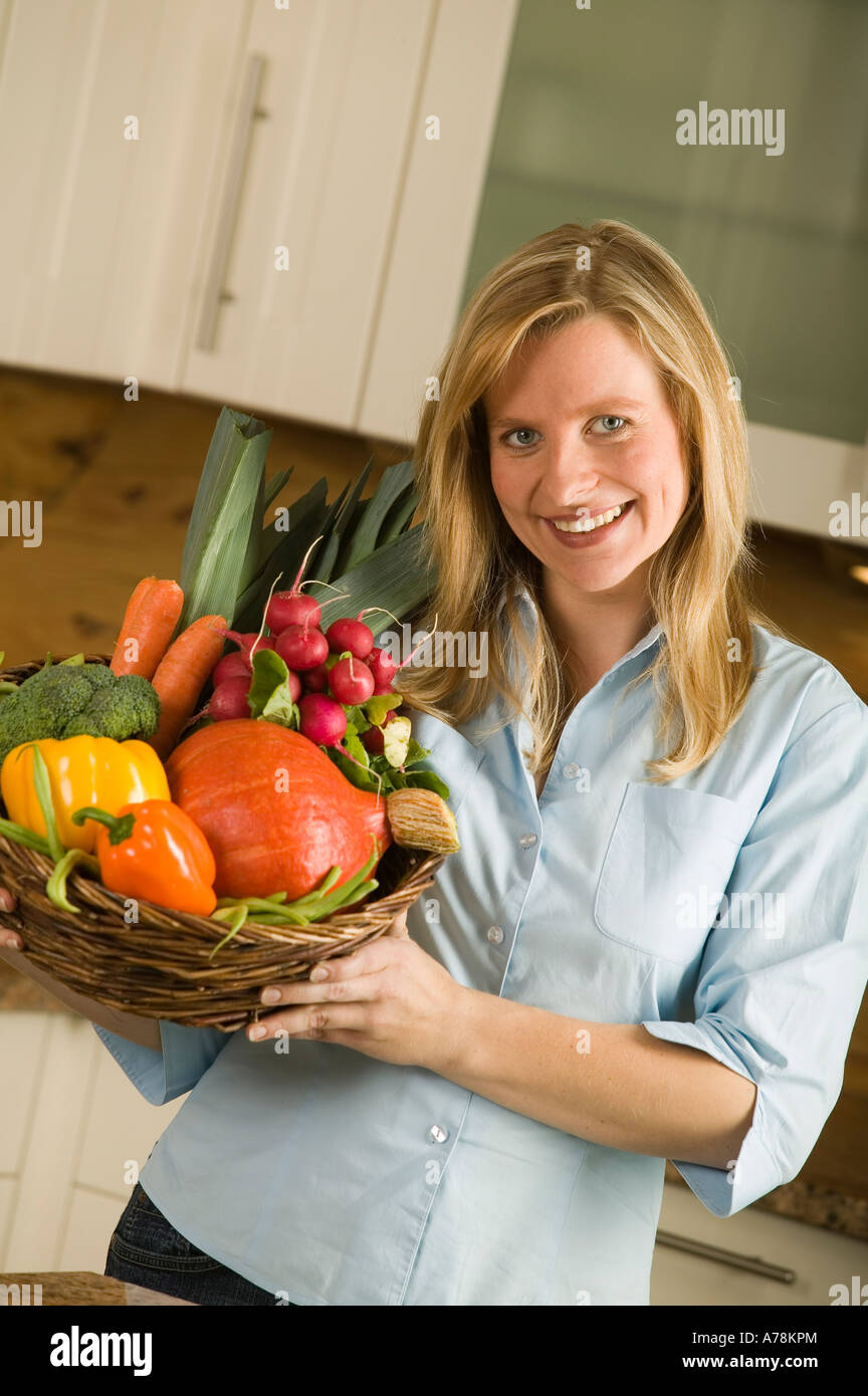 smiling woman in kitchen holding basket with organic vegetables fruit ...