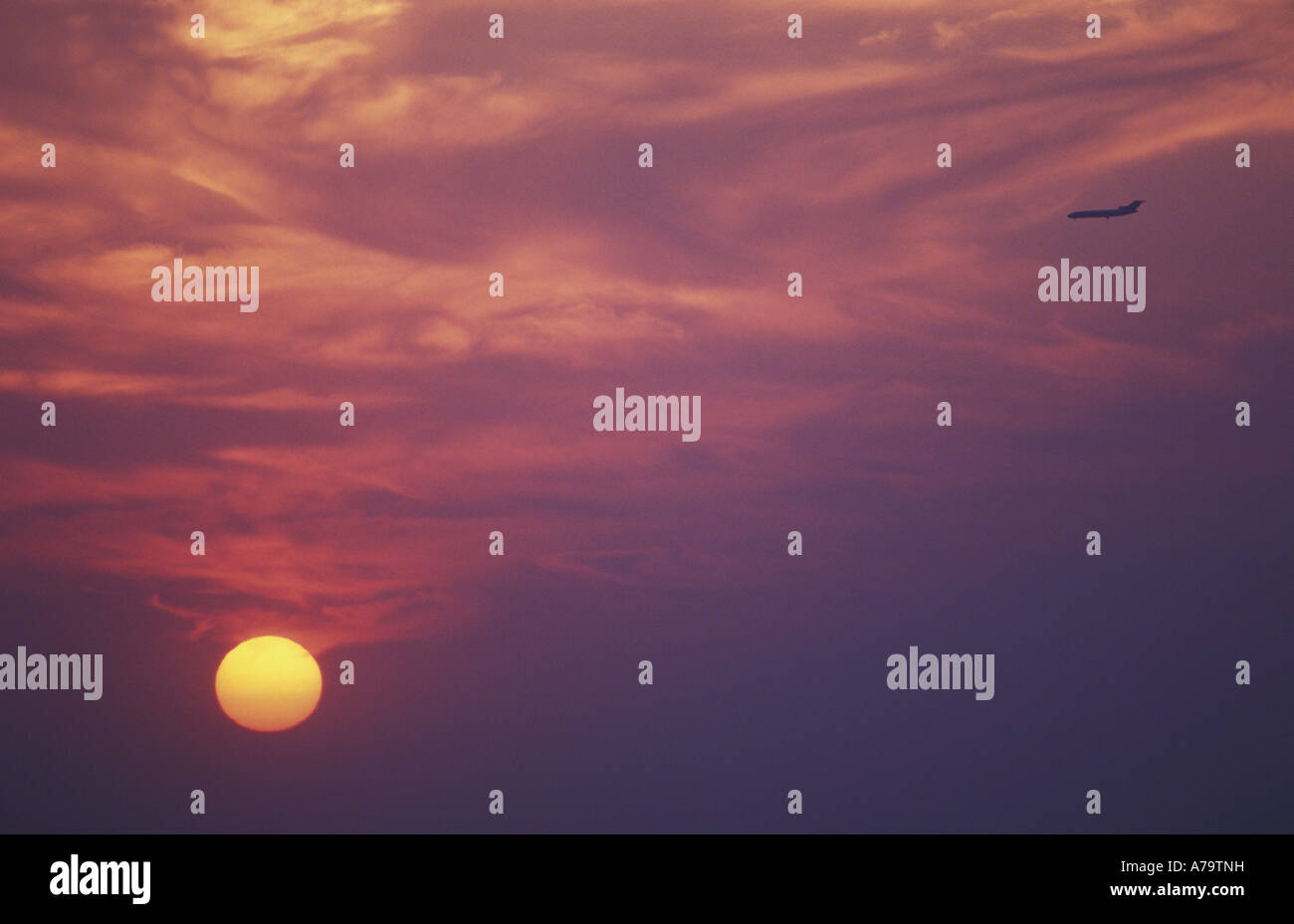 An airplane crosses the incredibly colorful late day setting sun Stock ...