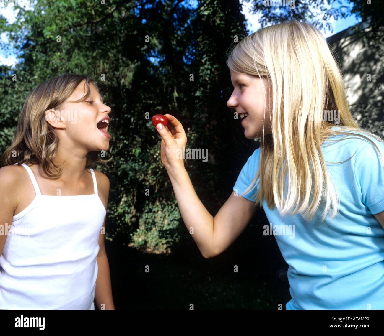 little girl feeding friend with cherry Stock Photo - Alamy