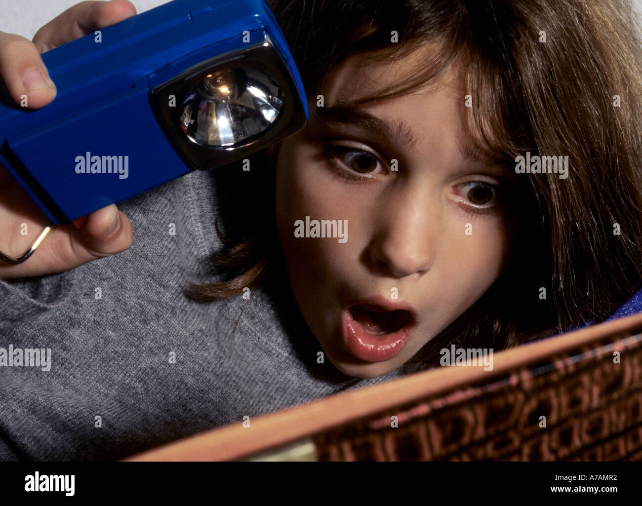 close up of young scared girl reading book by flashlight Stock Photo ...