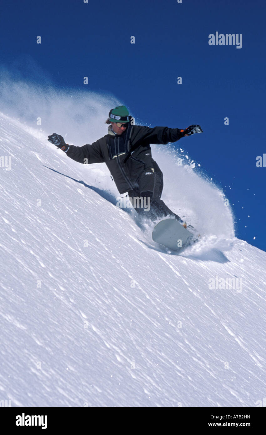 Snowboarder in a riding stance coming down a very steep slope in the ...