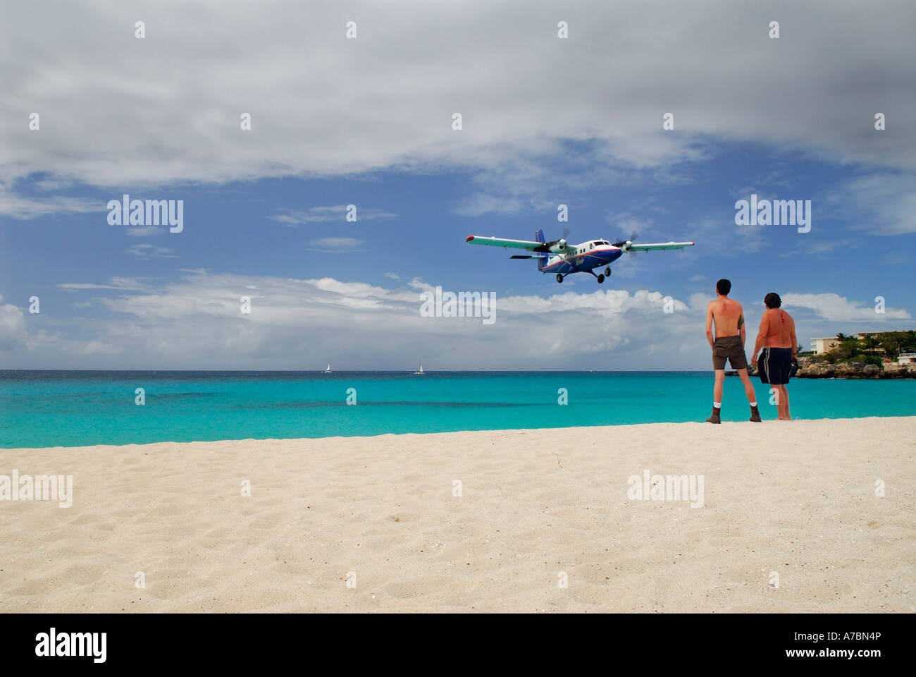 Two shirtless male beachgoers watch a plane land in St Maarten Princess ...