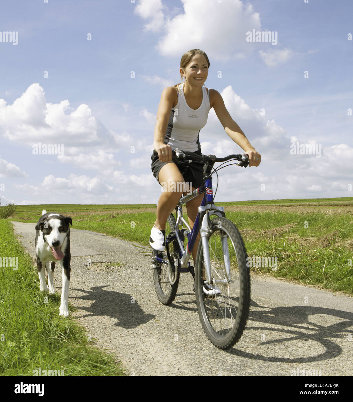 woman riding a bike - half breed dog running beside Stock Photo - Alamy