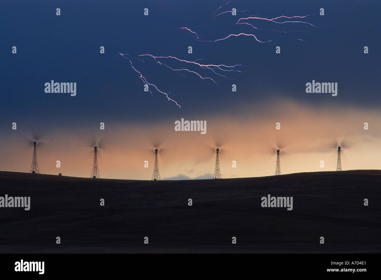 Lightning storm clouds passing over line of wind turbines representing ...