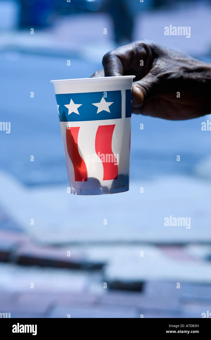 Hand of beggar, panhandler, holding out paper cup with US flag decor on ...