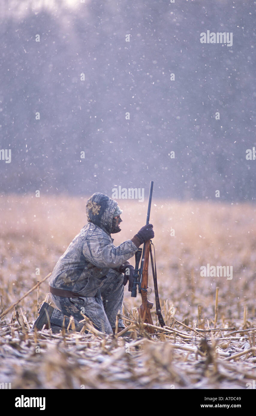 Hunter with a rifle in a corn field during an early snowfall Illinois ...