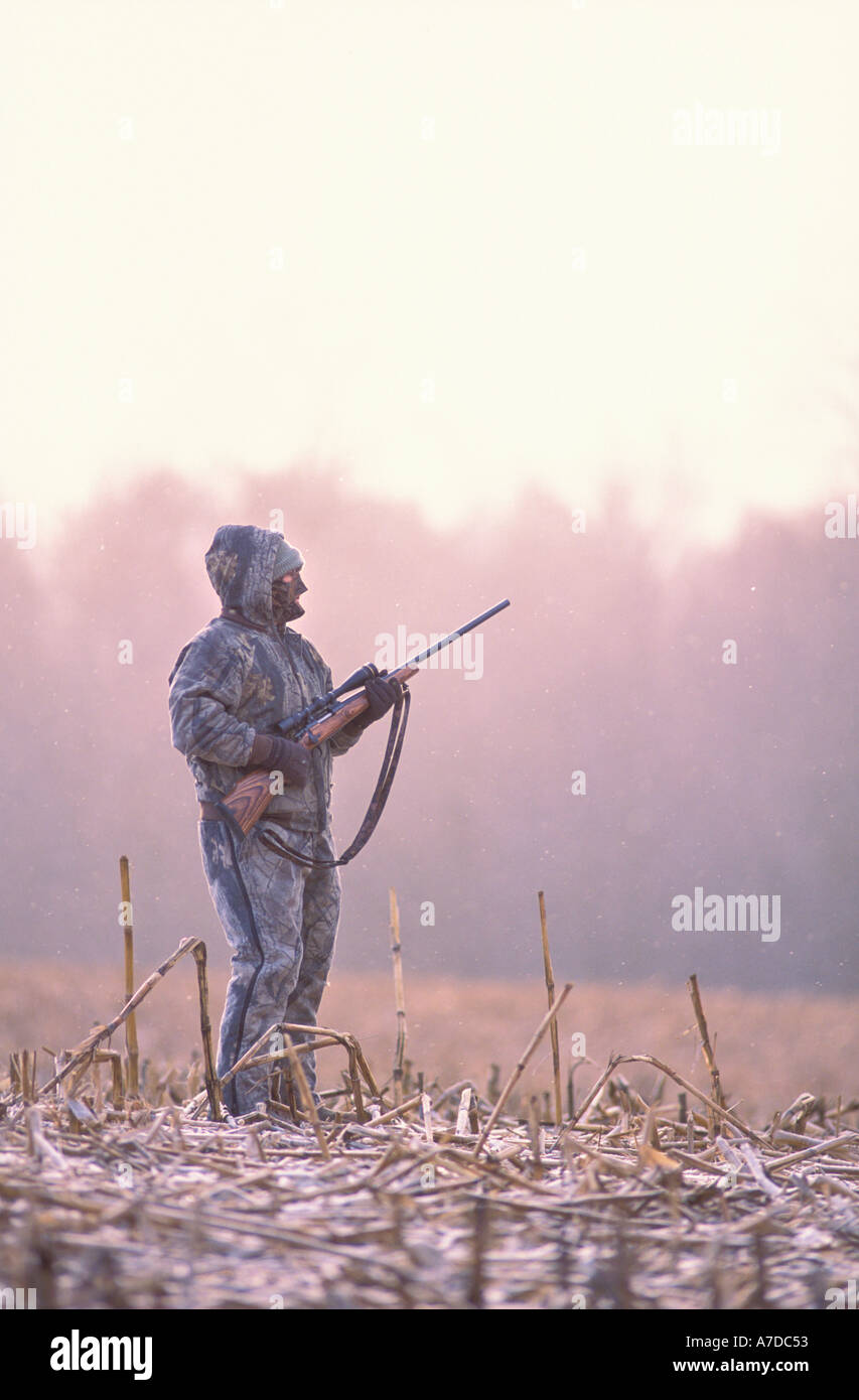 Hunter with a rifle in a corn field during an early snowfall Illinois ...