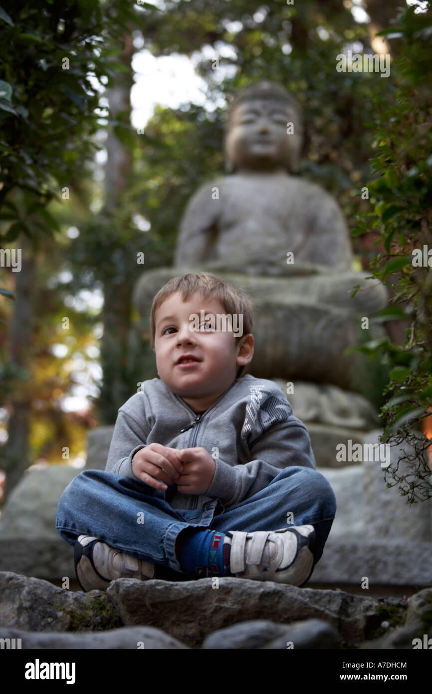 Young western boy child in contemplation in front of Buddha statue in ...