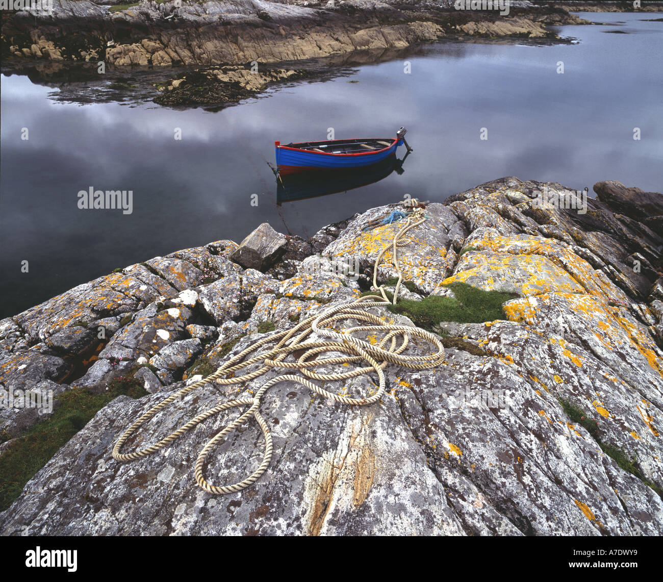 Moored boat and coiled mooring rope on rocks Loch Stockinish Harris ...