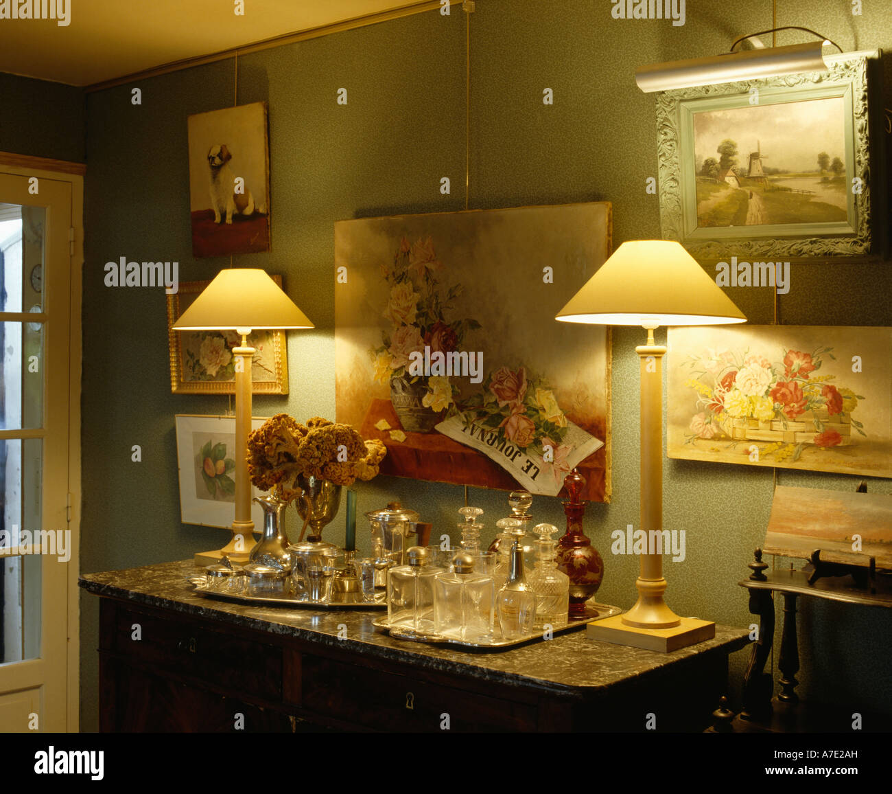 Lighted lamps and glass decanters on console table below pictures on ...