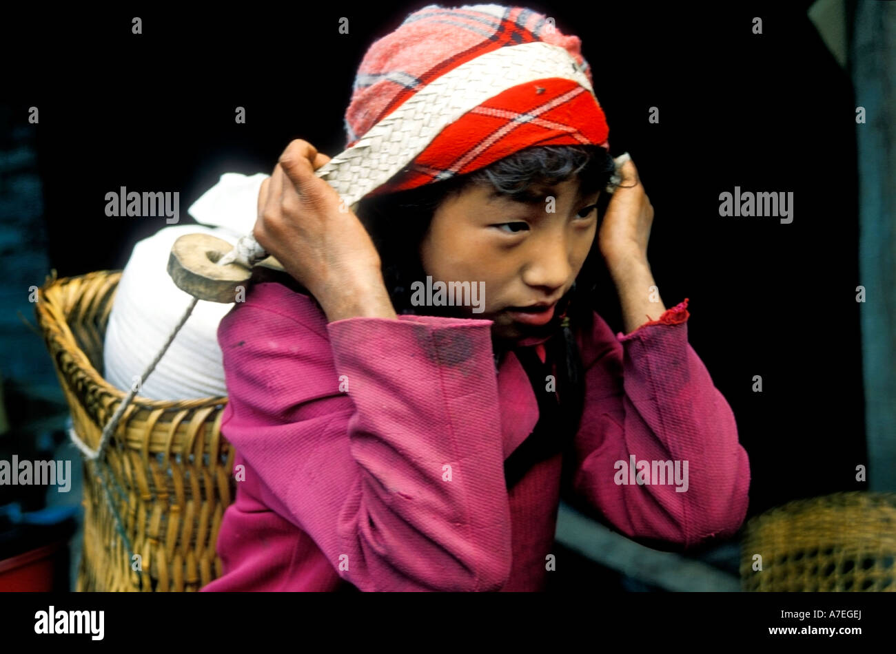 Young girl wearing a pink jacket carrying a sack of rice on her back ...