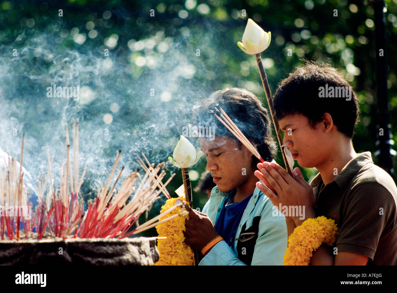 Two young men kneeling before a container of burning incense holding ...