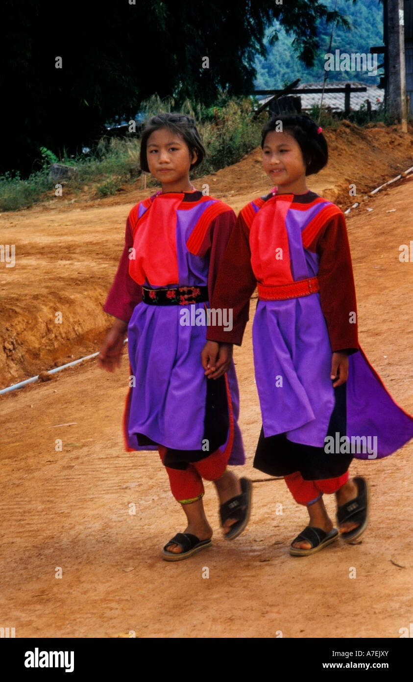 Two Lisu girls wearing traditional clothing walking down a mud road ...