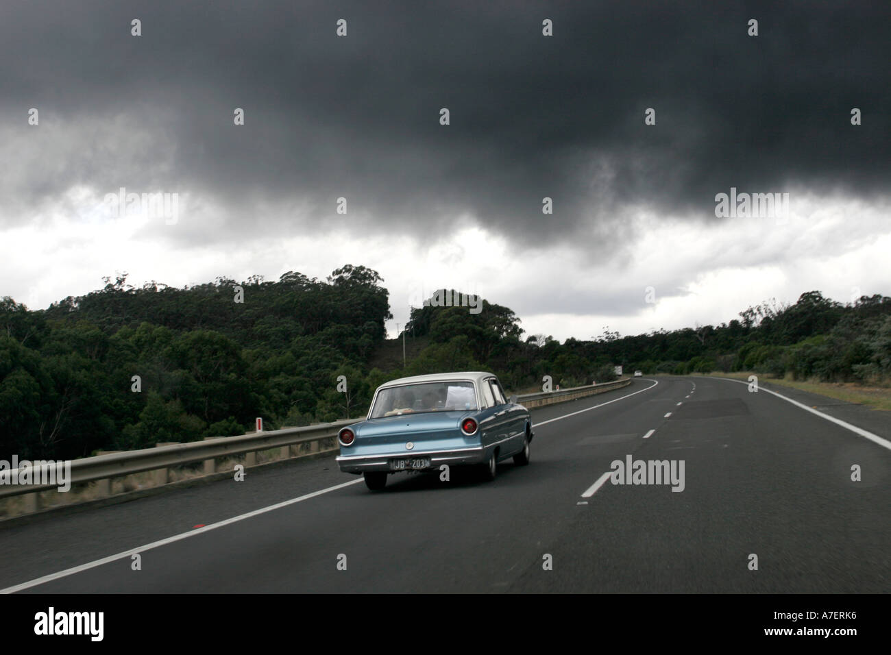 An early model Ford Falcon under stormy skies on the Hume highway ...