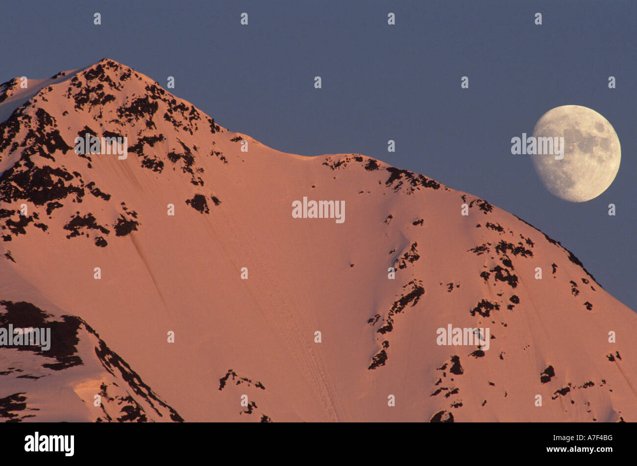 USA Alaska Gibbous moon rises above snow covered Kenai Range peaks ...