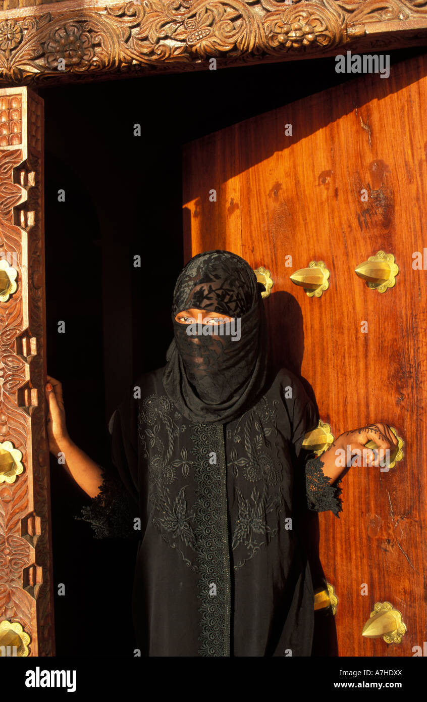 Swahili woman wearing traditional buibui standing at a Zanzibar door ...