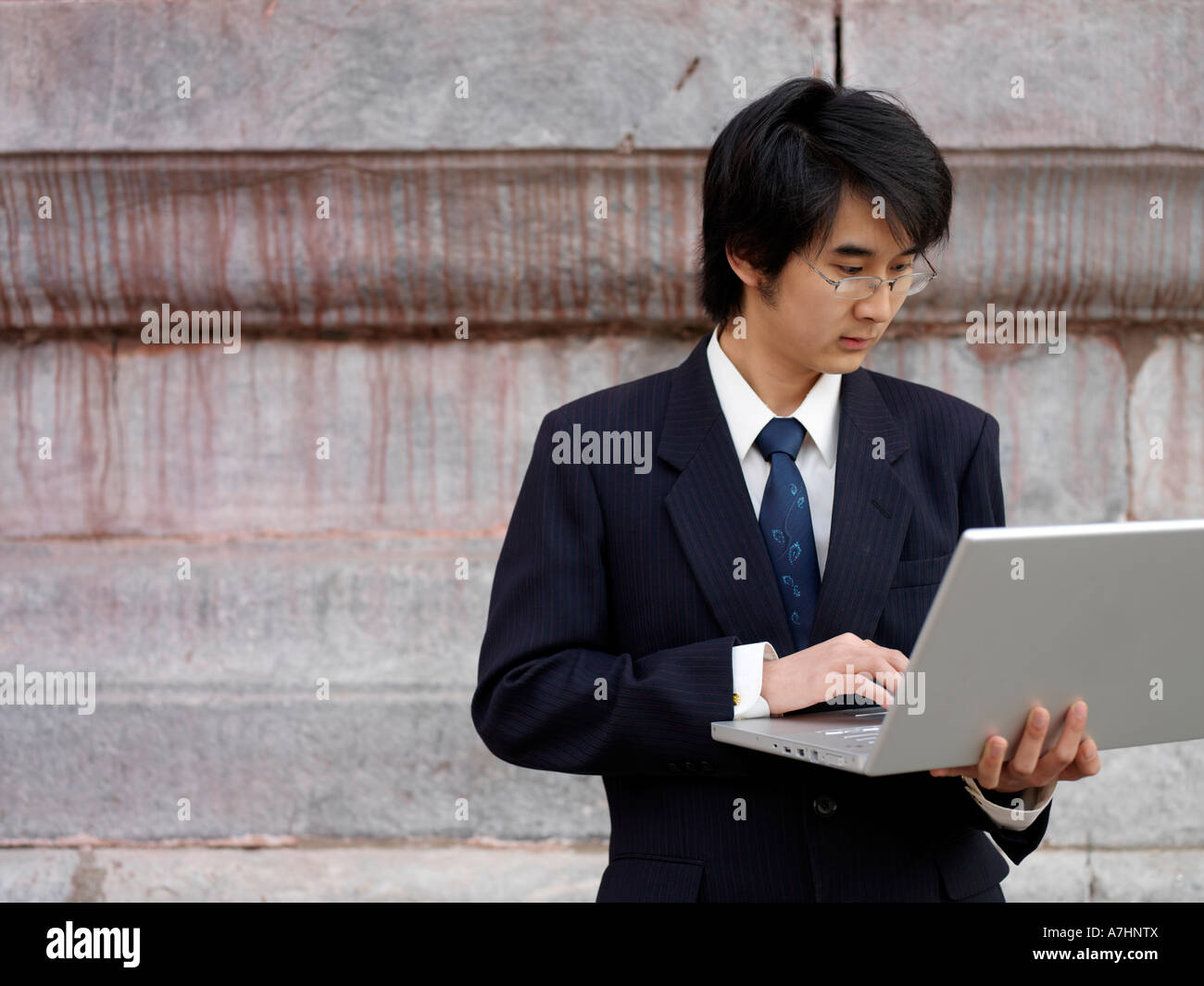 A young Chinese business man in a suit checking his email on his laptop ...