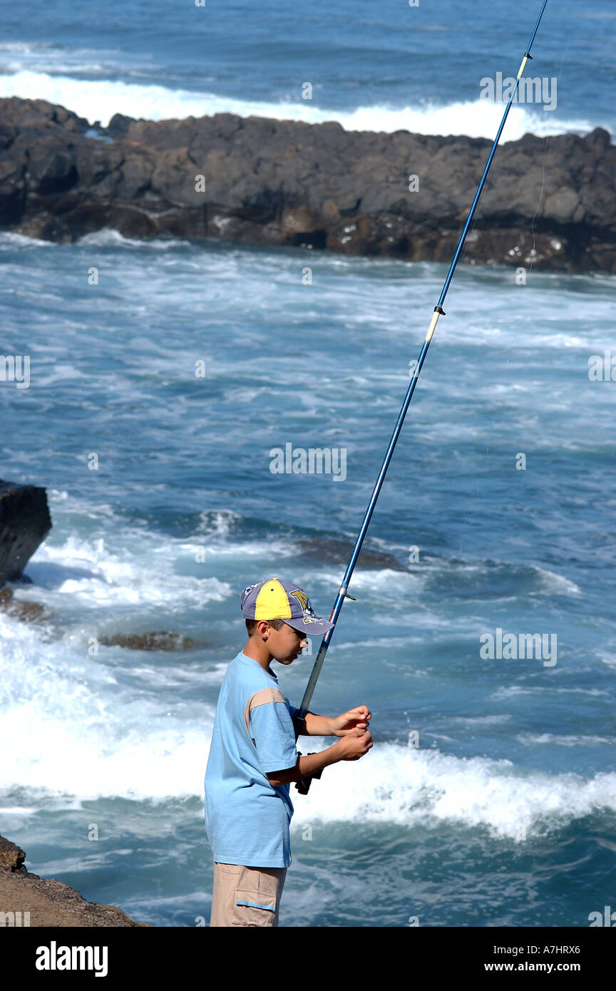 Boy in cap reeling in fishing rod trying to catch a fish with bait ...