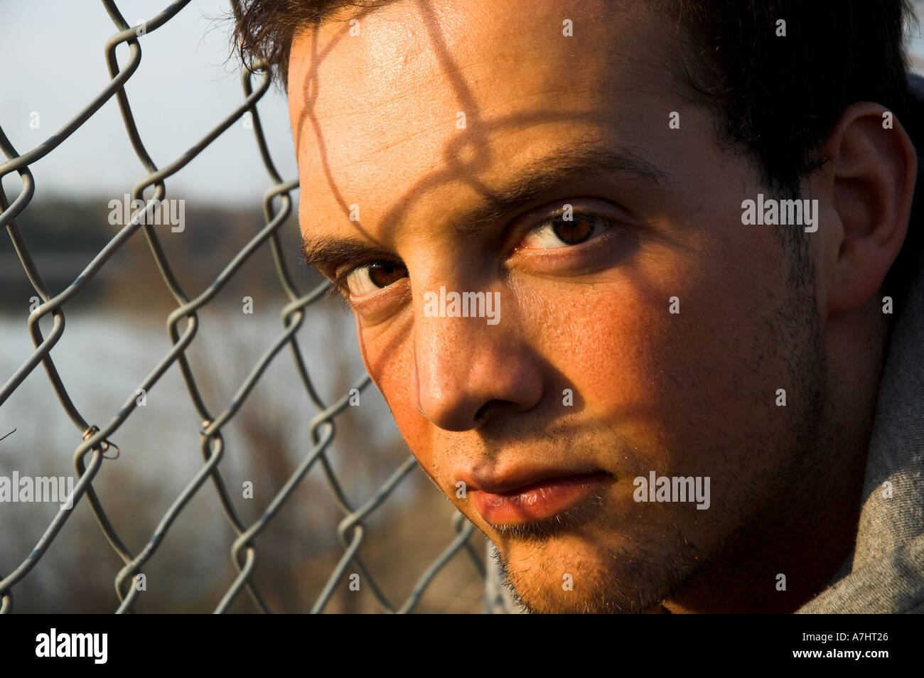 A young male looking at the camera with a shadow of a fence on his face ...