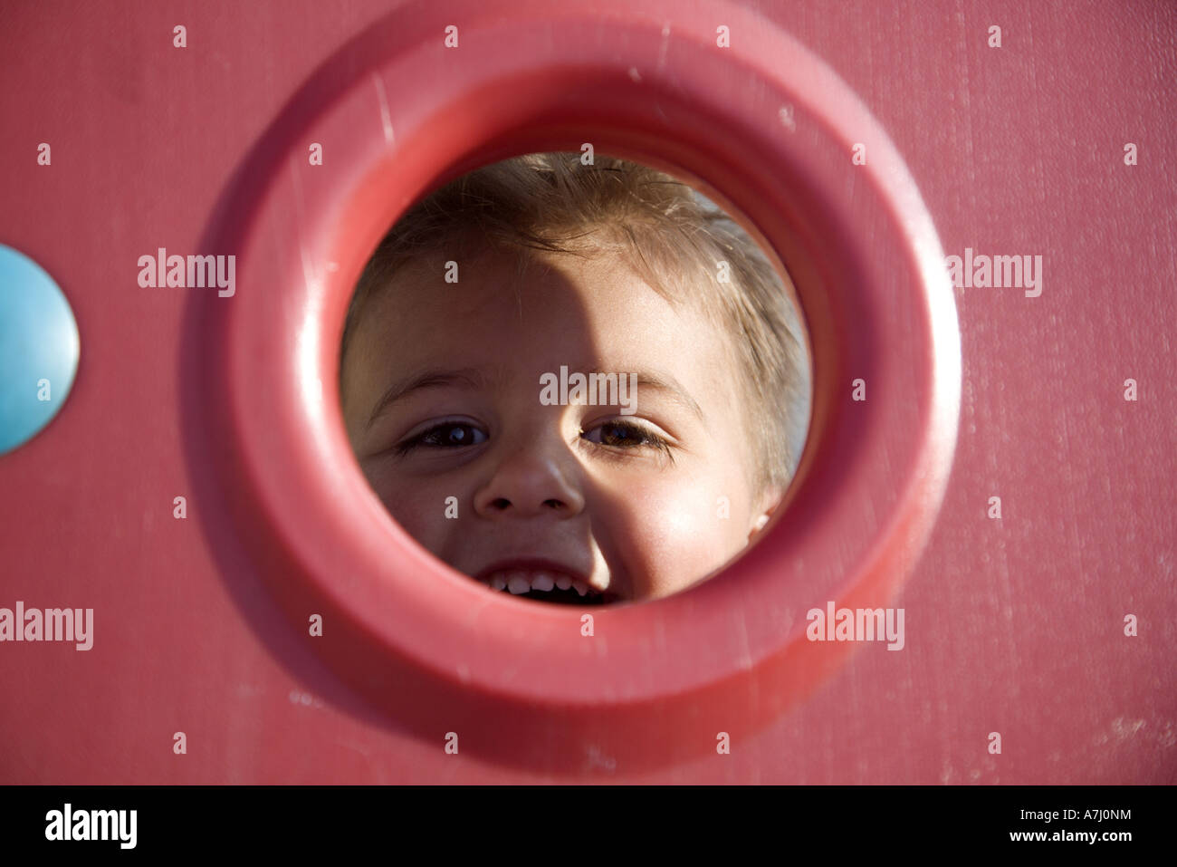 Two year old boy looking through hole in playing apparatus, Holland ...