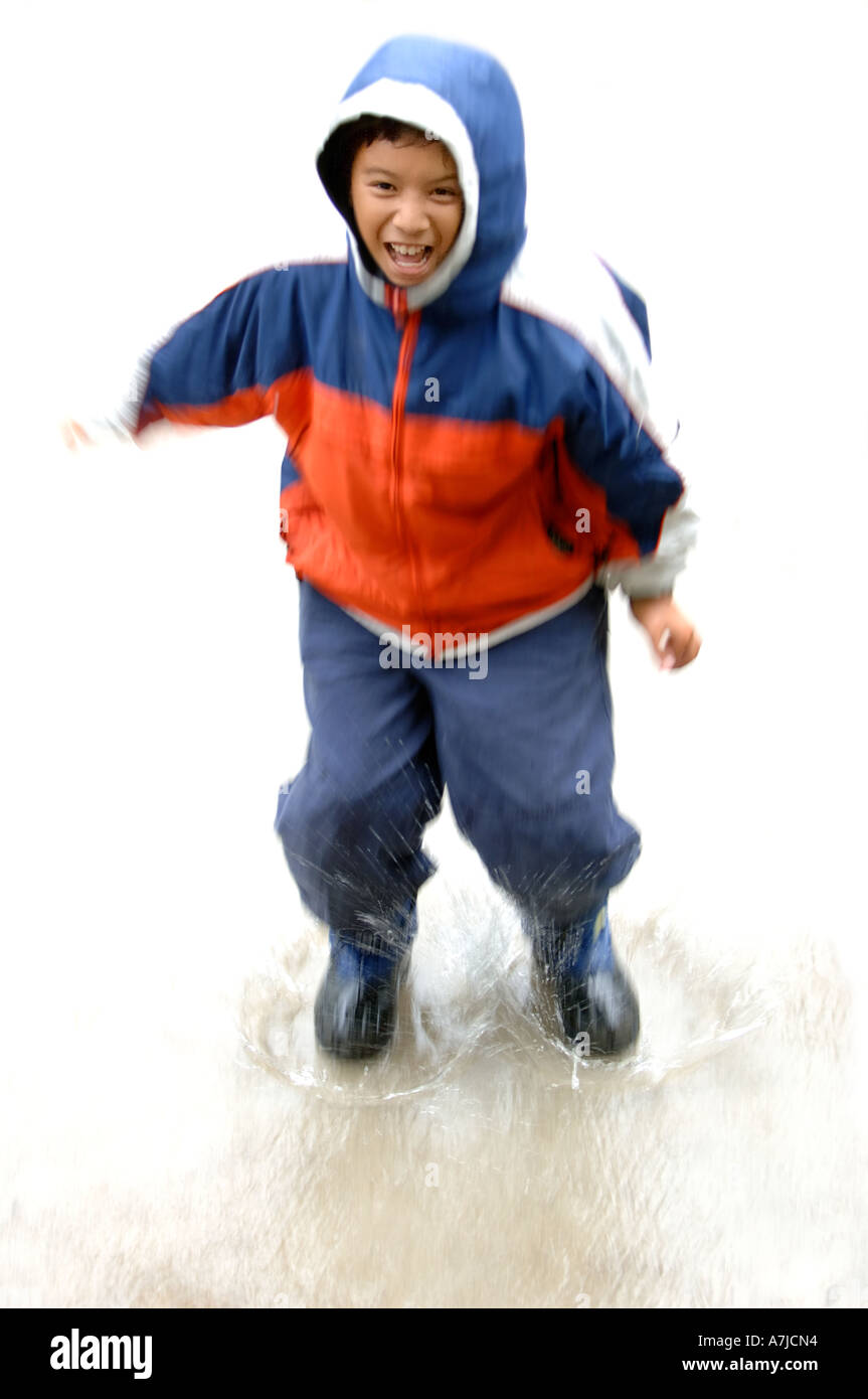 Boy (8-10) playing during bad weather and rain in puddle of water ...
